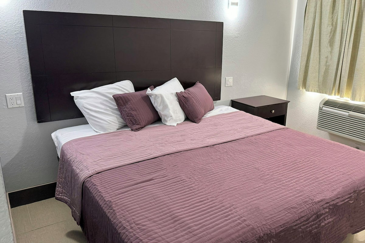 Uma cama com cabeceira, almofadas, mesa de cabeceira e ar condicionado.