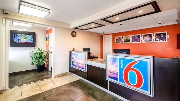 Uma área de recepção de hotel com um grande letreiro com o número '6', uma tela digital mostrando um mapa e um relógio na parede.