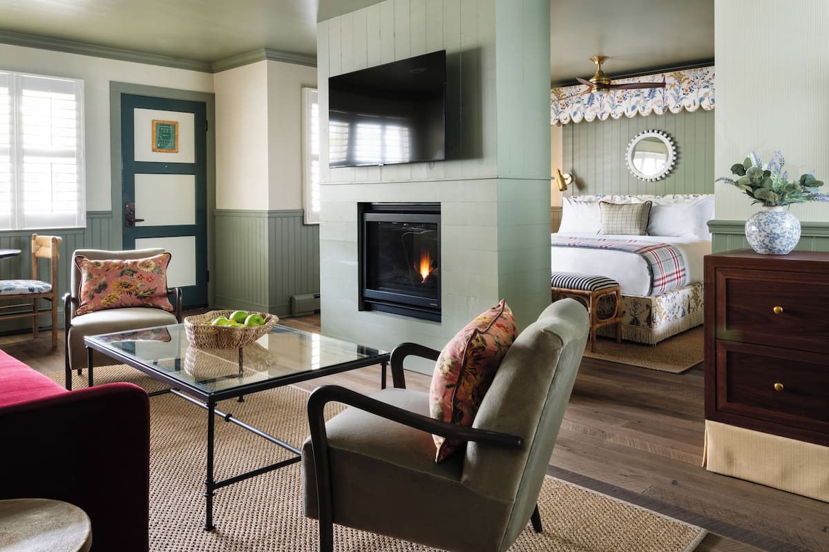 Uma sala de estar aconchegante com lareira, assentos confortáveis e uma cama com roupa de cama florida.