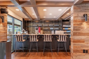 Uma área de bar moderna com detalhes em madeira, banquetas e um expositor de vidro.