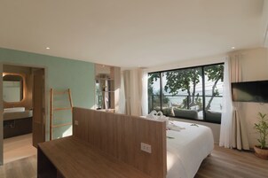 Quarto de hotel com cama, televisão, janela vista para o mar e banheiro com pia e espelho.
