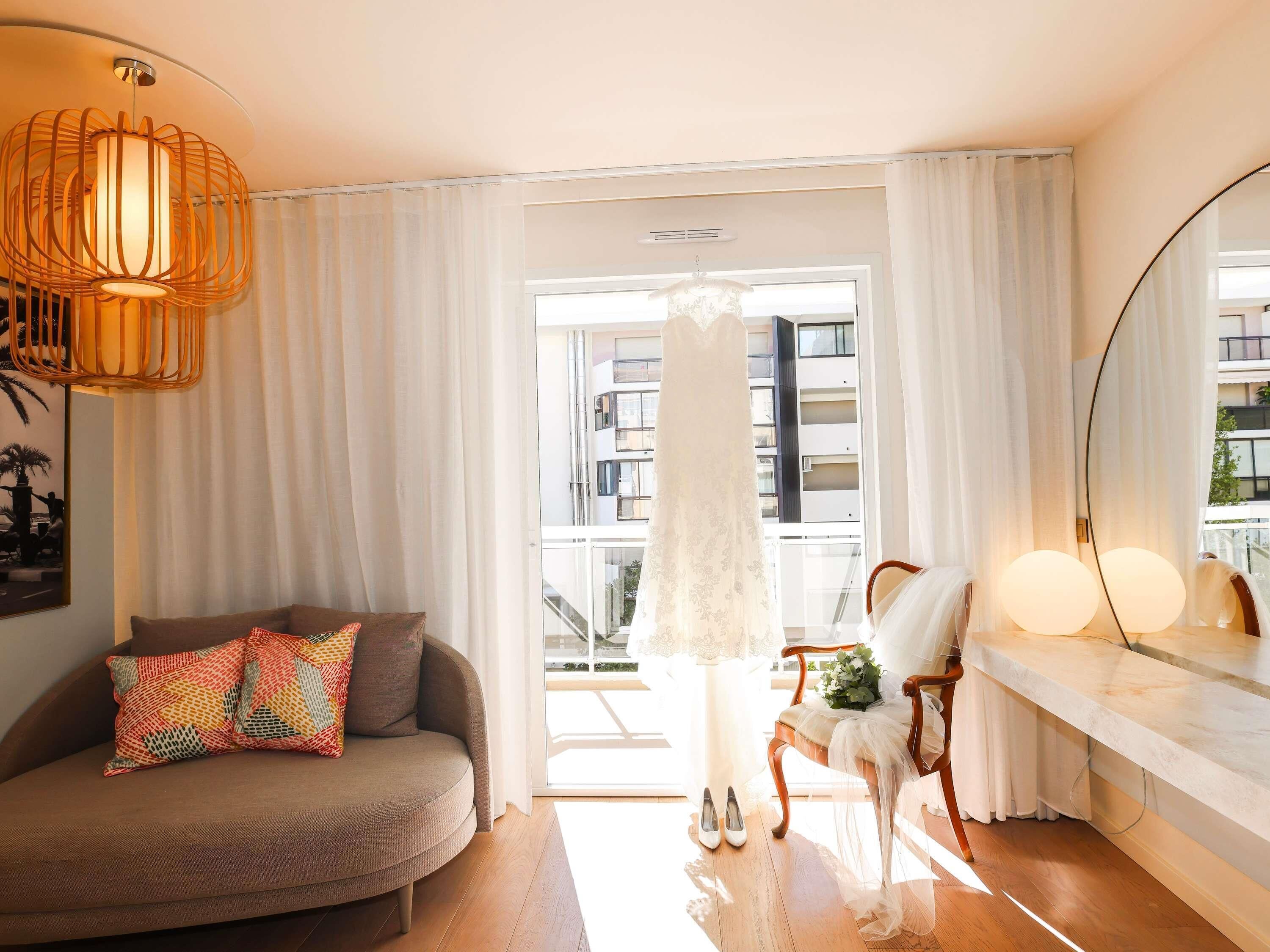 Uma sala de estar moderna com um sofá, uma poltrona com um buquê, uma luminária pendente e vista para um edifício.