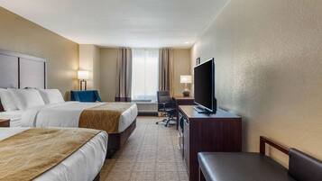 Quarto de hotel com duas camas, uma escrivaninha com televisão, uma cadeira e uma janela com cortinas.