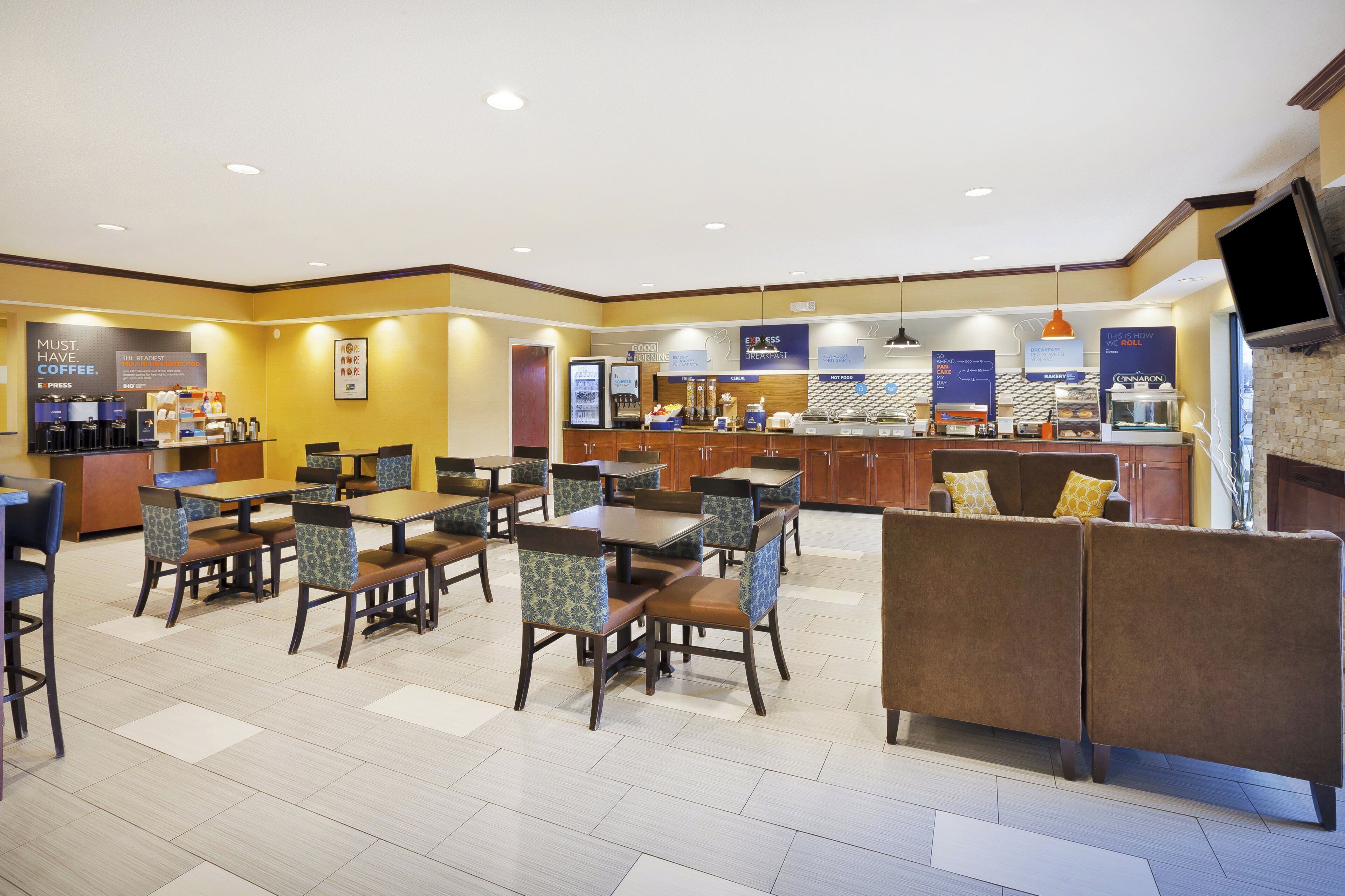 Espaço de café da manhã de hotel, com assentos, estação de café e balcão com opções de comida e bebida.