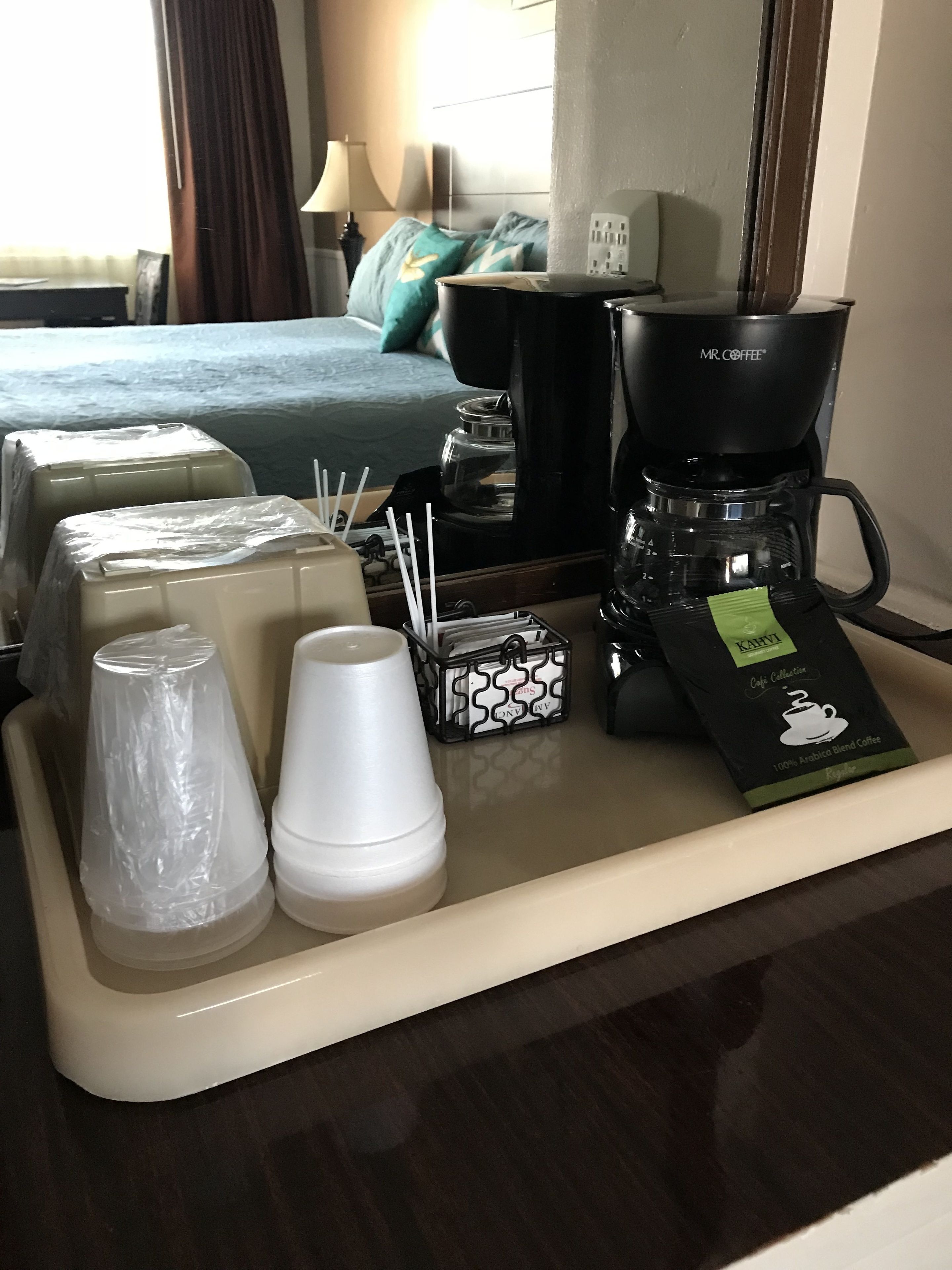 Quarto de hotel com cama, cafeteira e bandeja com chávenas de café e cápsula de café.