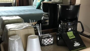 Quarto de hotel com cama, cafeteira e bandeja com chávenas de café e cápsula de café.
