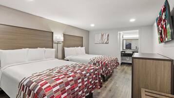 Quarto de hotel com duas camas, uma escrivaninha, um espelho e uma televisão na parede.