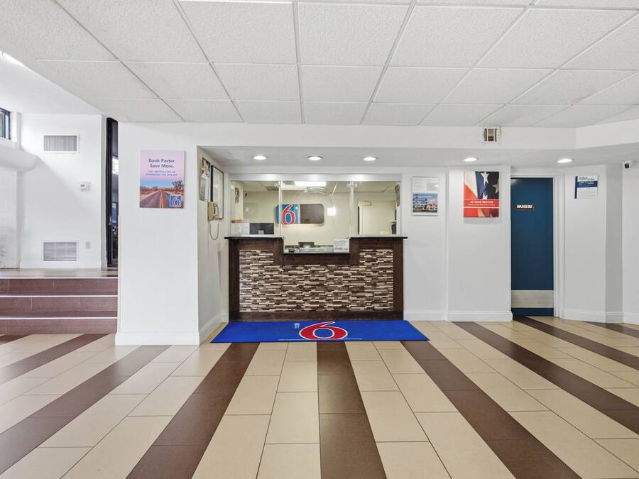 Uma área de recepção com balcão, um tapete azul com logotipo e uma escadaria para um andar superior.