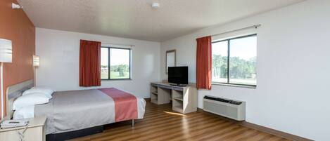 Quarto de hotel com cama, escrivaninha, televisão e janelas amplas.