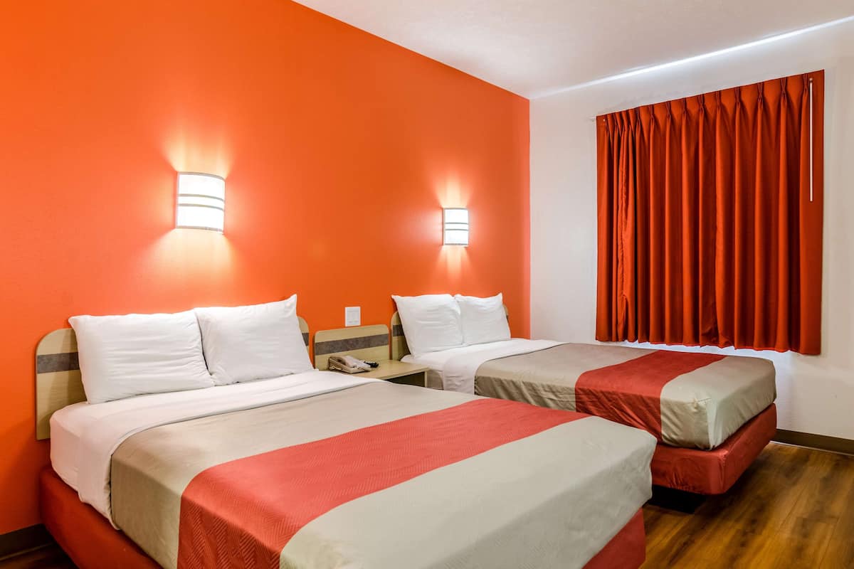 Quarto de hotel com duas camas, paredes laranja e uma janela com cortinas vermelhas.