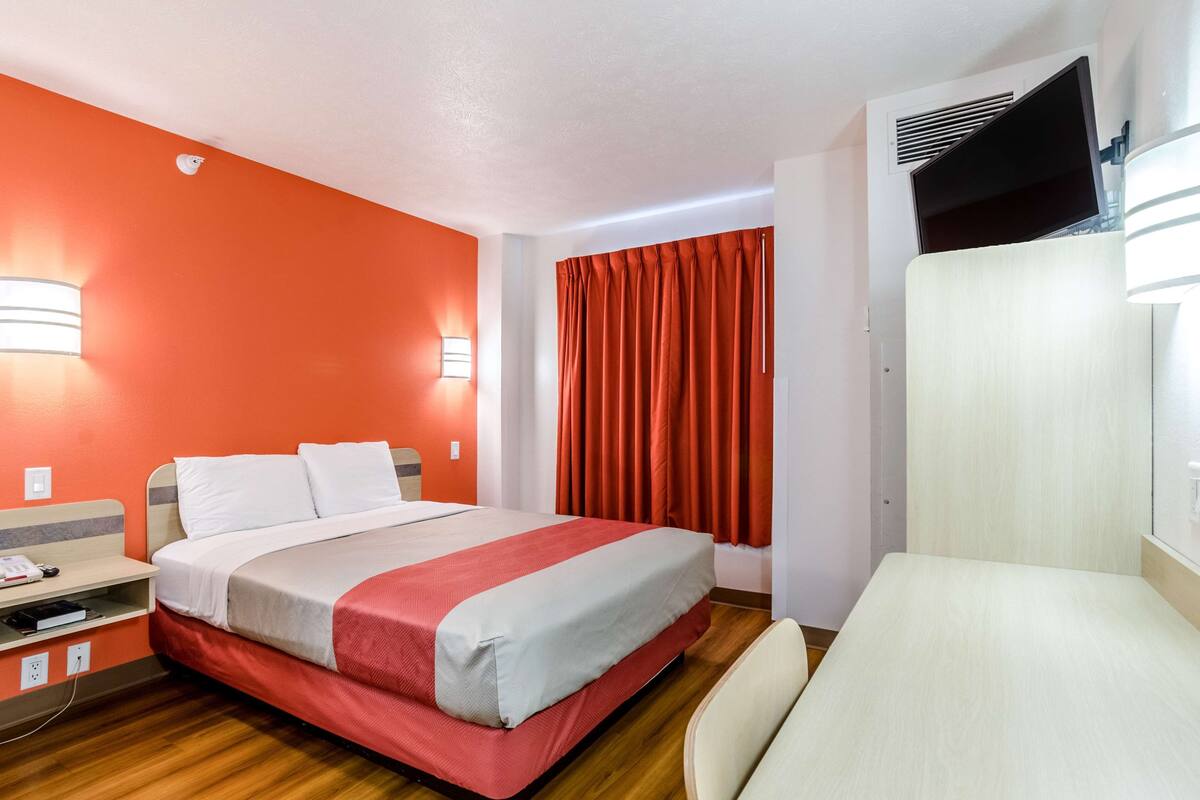 Quarto de hotel com cama, mesa de cabeceira e televisão em suporte.