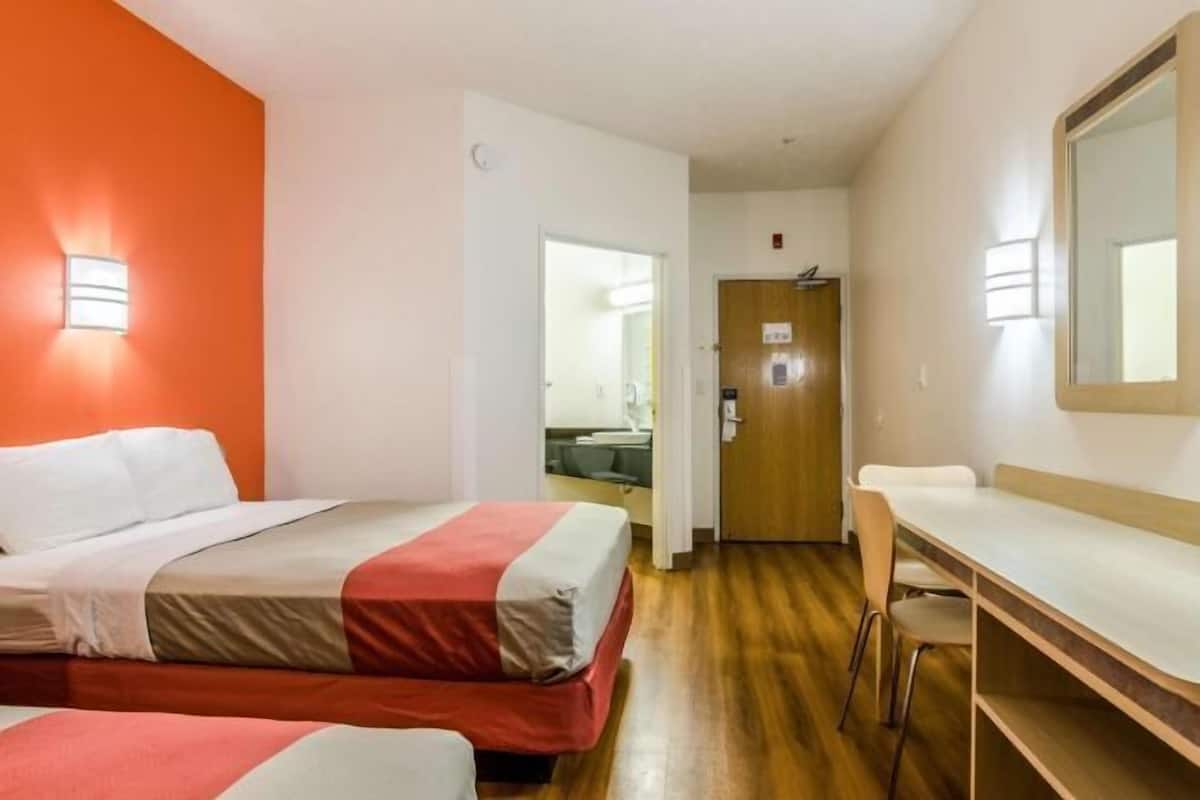 Quarto de hotel com duas camas, uma escrivaninha e uma cadeira.