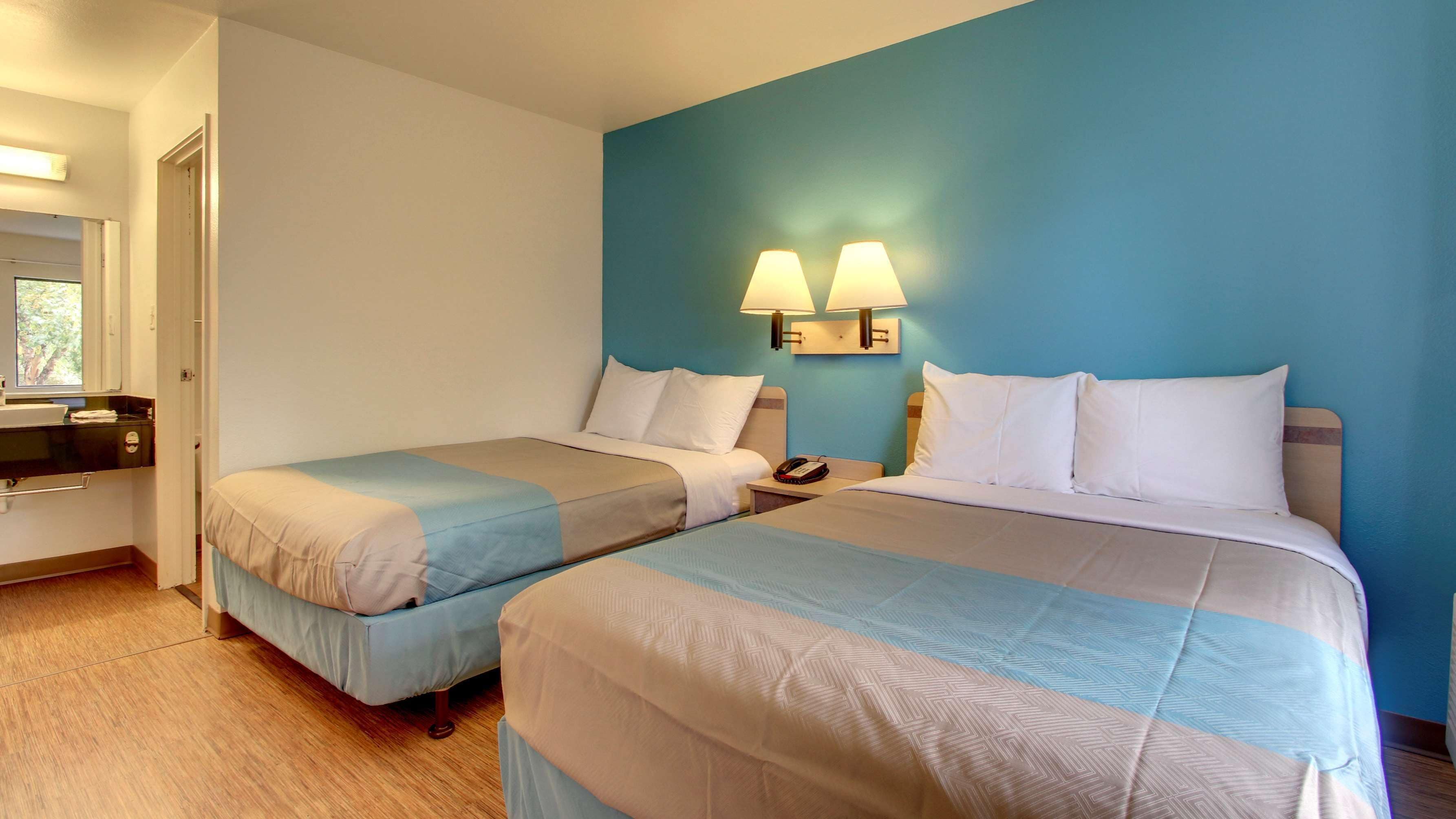 Quarto de hotel com duas camas, banheiro e janela.