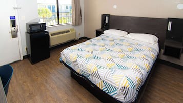 Quarto de hotel com cama, escrivaninha com micro-ondas, aquecedor e janela com vista para edifícios.