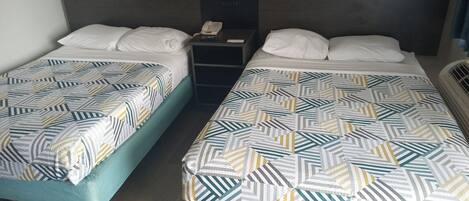 Duas camas de solteiro com roupa de cama estampada, uma mesinha de cabeceira com telefone e uma cabeceira escura.