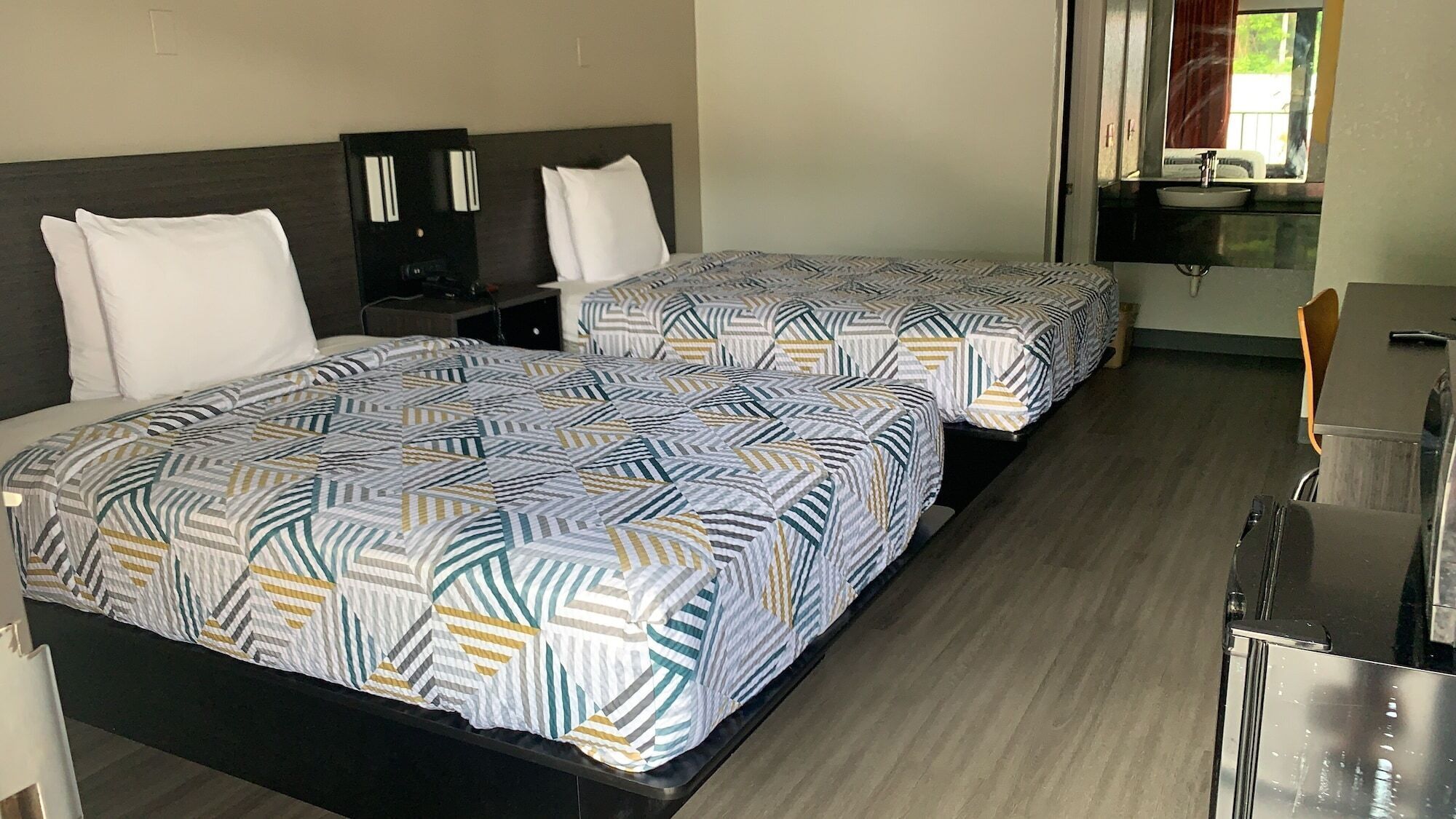 Quarto de hotel com duas camas, uma escrivaninha, uma cadeira, um espelho e uma janela.