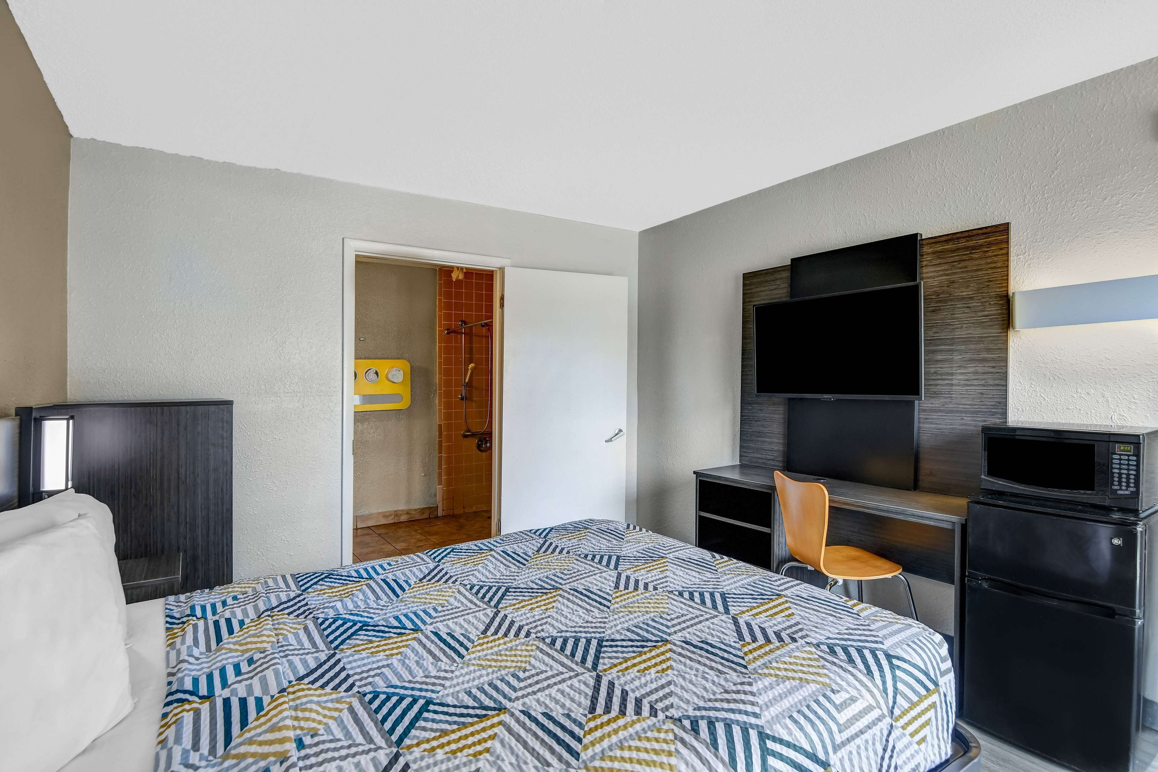 Quarto de hotel com cama, escrivaninha com cadeira, televisão e frigorífico.