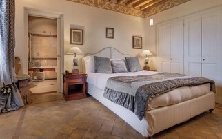 Quarto com uma cama grande, duas mesas de cabeceira com abajures, um criado-mudo de madeira, um guarda-roupa e um banheiro com chuveiro e vaso sanitário à vista.