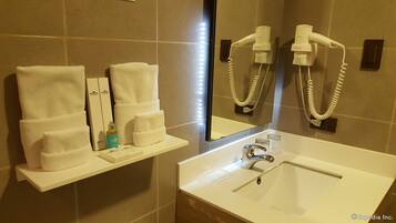 Casa de banho de hotel com lavatório branco, espelho e toalheiro com várias toalhas e produtos de higiene pessoal.