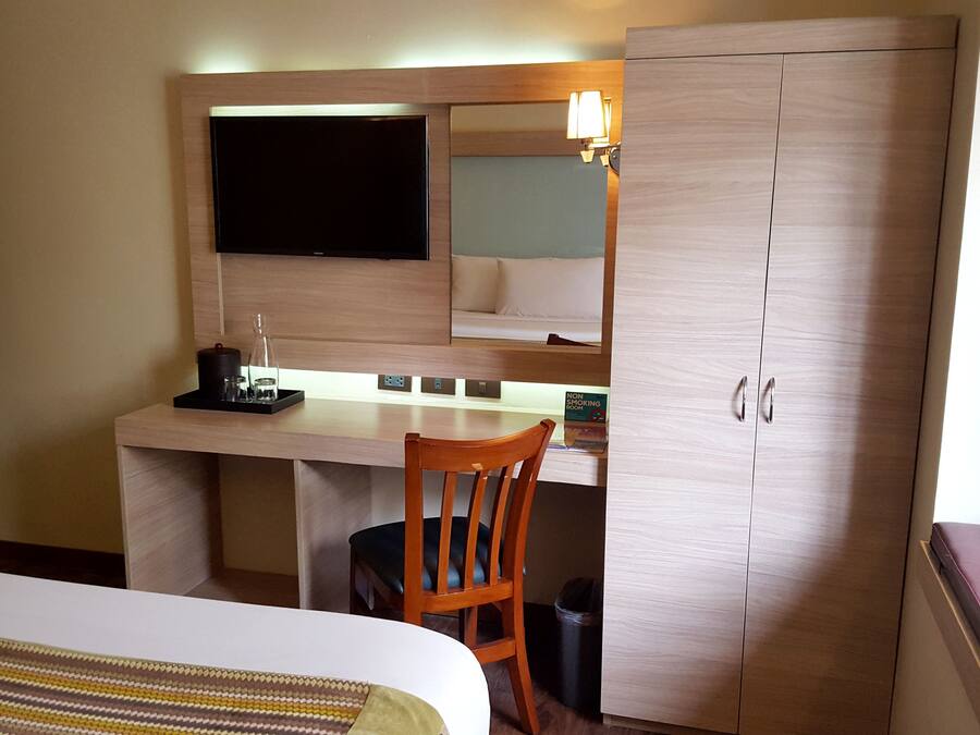 Quarto de hotel com cama, escrivaninha com computador, cadeira e guarda-roupa.