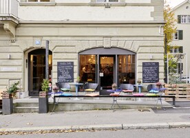 Um café com mesas ao ar livre, cardápio na lousa e entrada de um edifício.