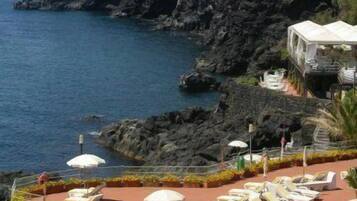 Um hotel à beira-mar com um terraço de espreguiçadeiras e guarda-sóis, com vista para o mar e falésias rochosas.