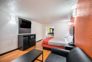 Quarto de hotel compacto com cama, escrivaninha, televisão e cozinha compacta.