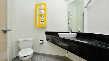 Um banheiro pequeno com vaso sanitário, pia e espelho. Há um porta-toalhas amarelo com três toalhas.
