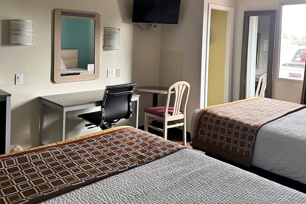Quarto de hotel com duas camas, uma escrivaninha com cadeira, televisão na parede e janela com vista para o exterior.