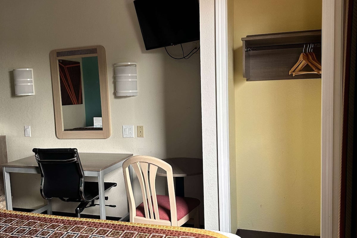 Quarto com escrivaninha, duas cadeiras, espelho, televisão na parede e cabideiro.