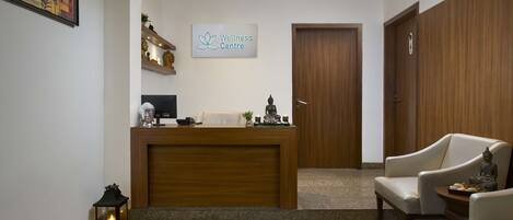 Uma área de recepção com uma mesa de madeira, uma placa com a inscrição "Wellness Centre" e uma estátua à direita.