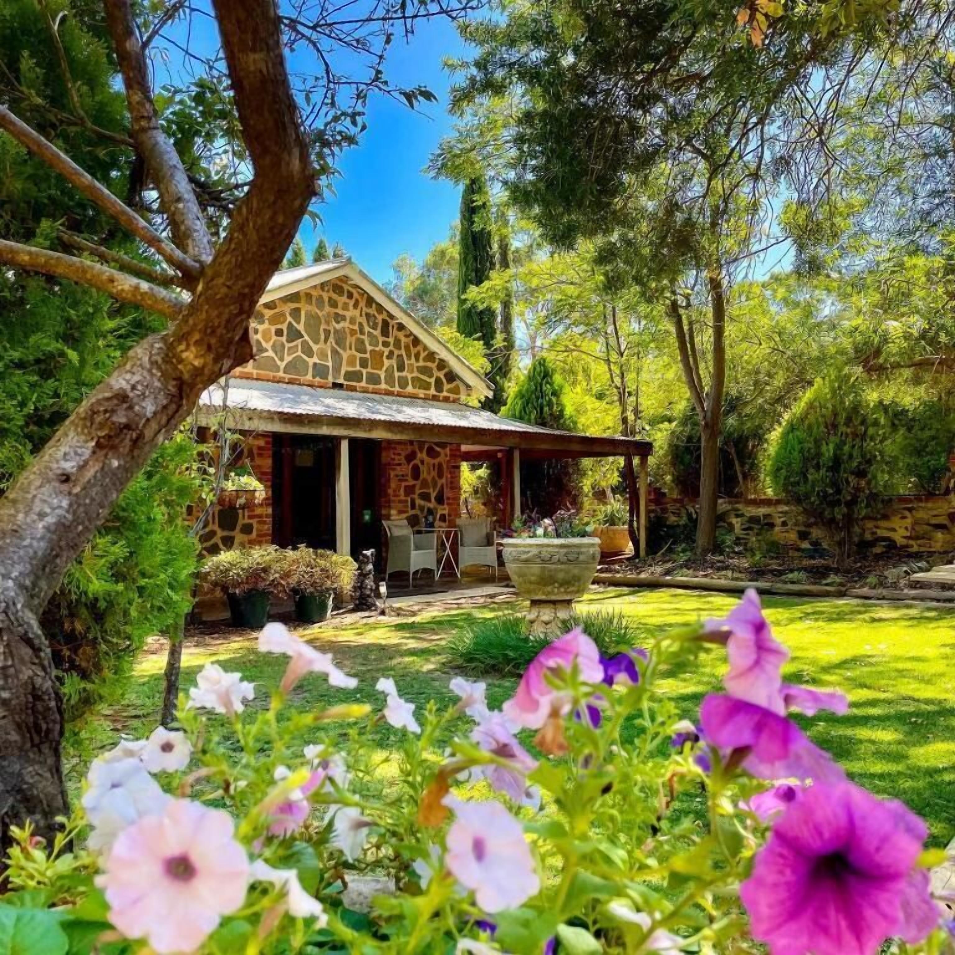 Uma casa com fachada de pedra, varanda coberta e jardim com plantas floridas.