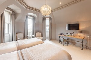 Quarto de hotel com duas camas, uma escrivaninha, uma cadeira, televisão e um candelabro.