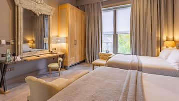 Quarto de hotel com duas camas, um espelho grande, uma escrivaninha com abajur, um guarda-roupa e vista para o exterior.