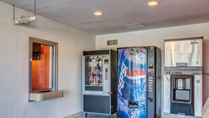 Uma área de distribuição automática com refrigerador de Pepsi, dispensador de gelo e placa de atendimento noturno.