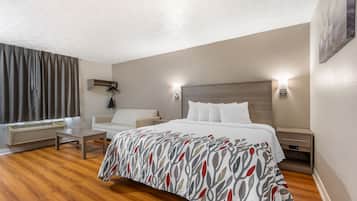 Quarto de hotel com cama, mesas de cabeceira, escrivaninha, cadeira, cabideiro e janela com cortinas.
