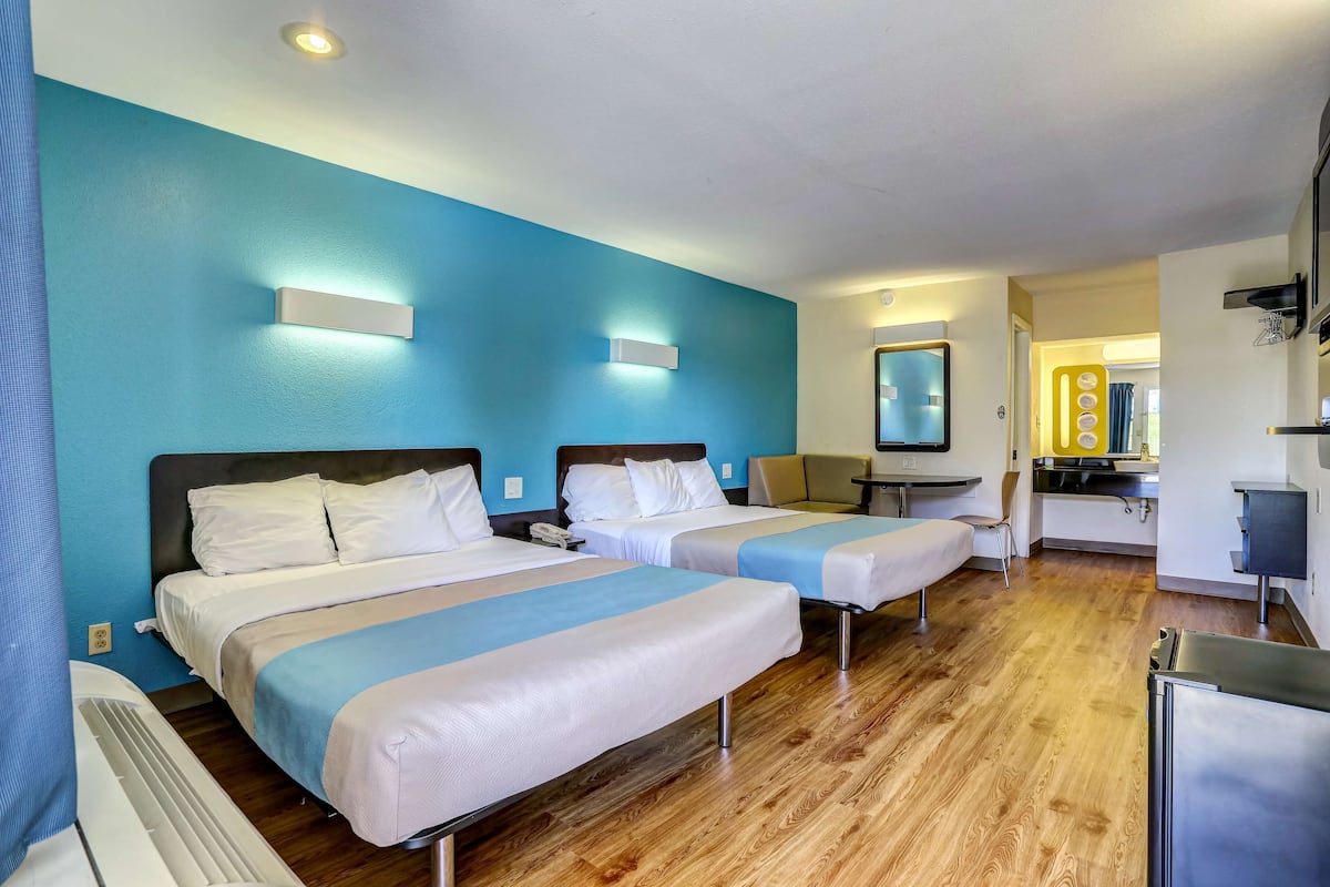 Quarto de hotel com duas camas, uma kitchenette pequena e um banheiro visível ao fundo.