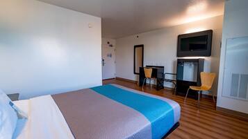 Quarto de hotel com cama, escrivaninha, cadeira, televisão e cabideiro.