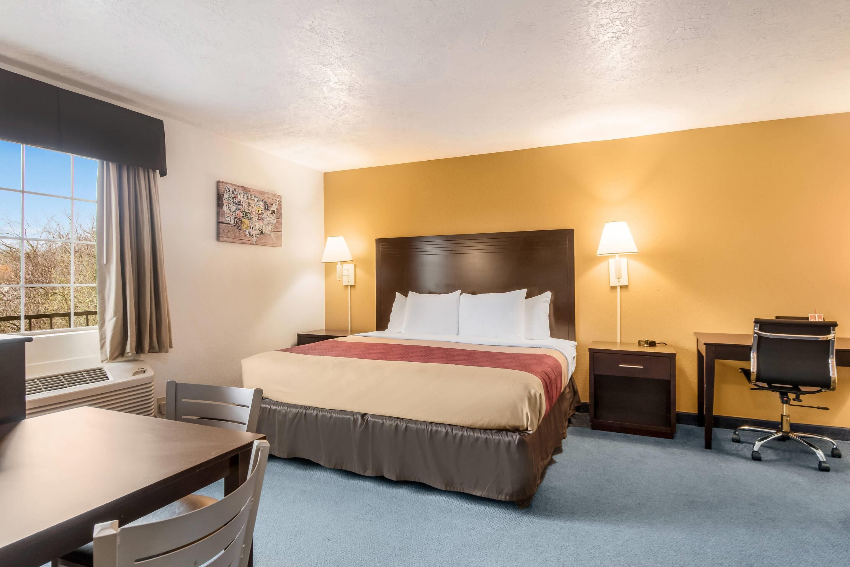 Quarto de hotel com cama, escrivaninha, cadeira e duas luminárias de cabeceira.