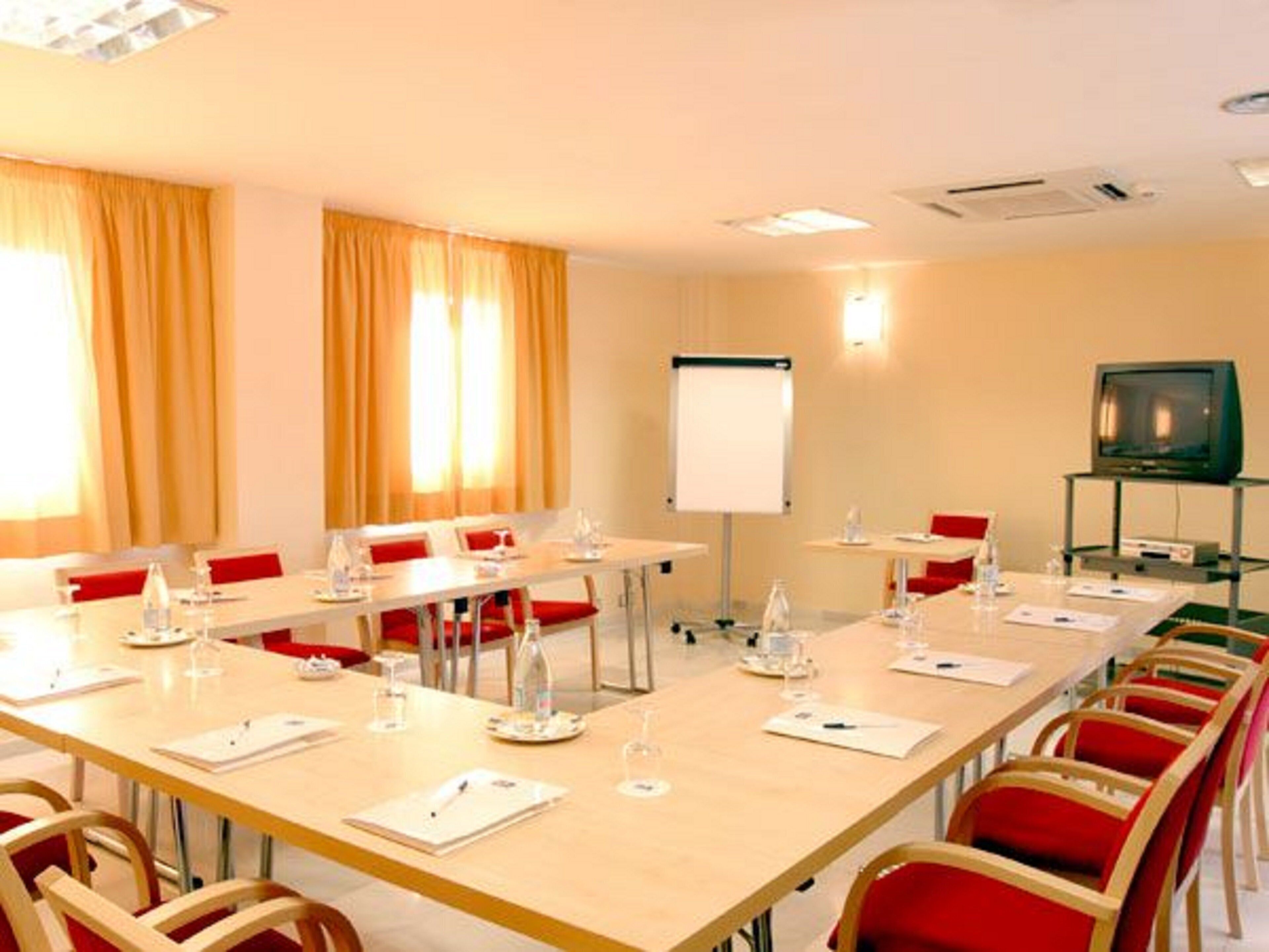 Uma sala de conferência com uma mesa comprida, cadeiras, um quadro branco e uma televisão.