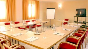 Uma sala de conferência com uma mesa comprida, cadeiras, um quadro branco e uma televisão.