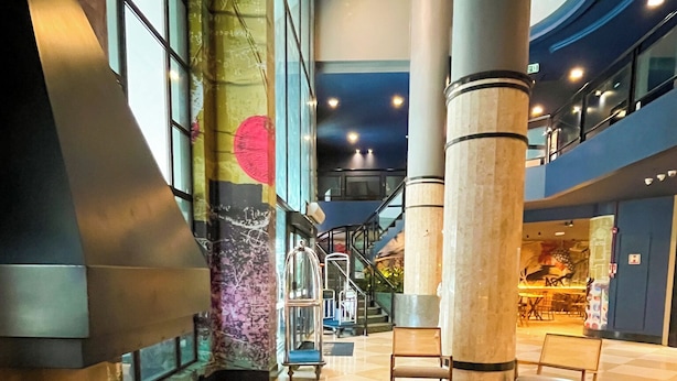 Um hall amplo com uma coluna grande, parede de vidro e área de estar com mesas e cadeiras.