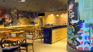 Um espaço de bar moderno com mobiliário de madeira, um mural colorido e um pilar central com design floral.