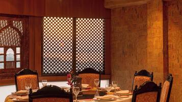 Uma sala de jantar com uma mesa posta para quatro pessoas, cadeiras elaboradas e uma janela decorativa com padrão em treliça.