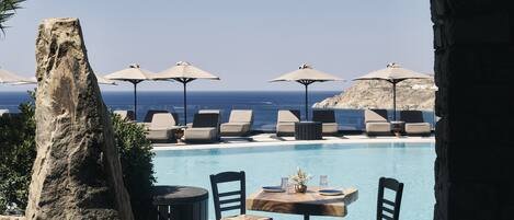Área da piscina com espreguiçadeiras e guarda-sóis, com vista para o mar.