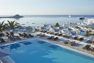 Um resort com área de piscina, espreguiçadeiras e vista para o mar e barcos.