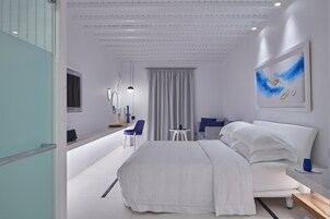 Quarto de hotel moderno com uma cama grande, uma escrivaninha com cadeira, uma mesinha e um quadro na parede.