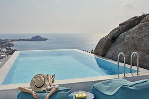 Piscina com vista para o mar, uma rocha à direita e uma pessoa relaxando.