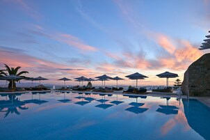 Piscina com espreguiçadeiras e guarda-sóis, refletindo o céu.