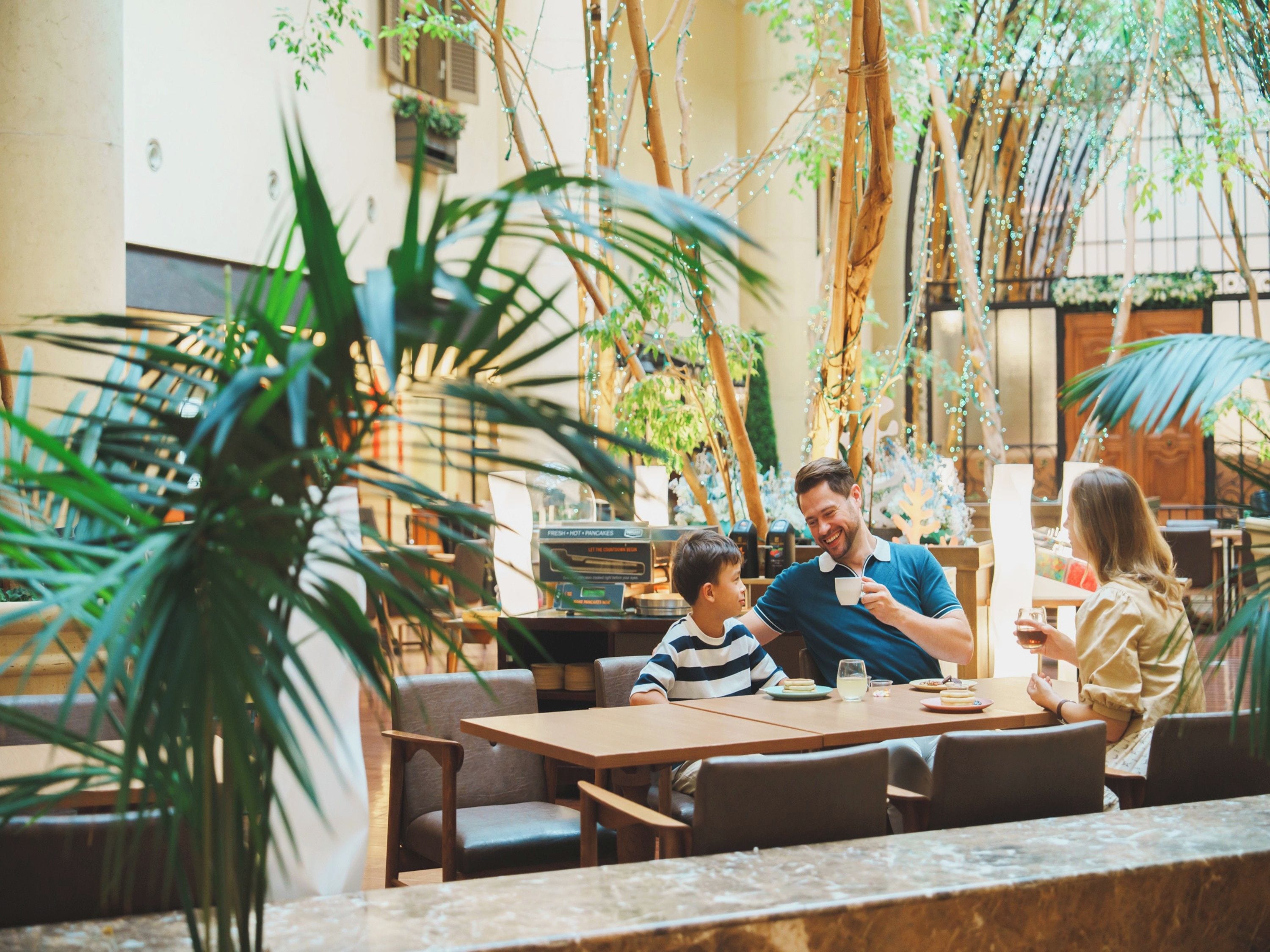 Espaço de refeições interno com mesas, cadeiras e plantas em vasos.